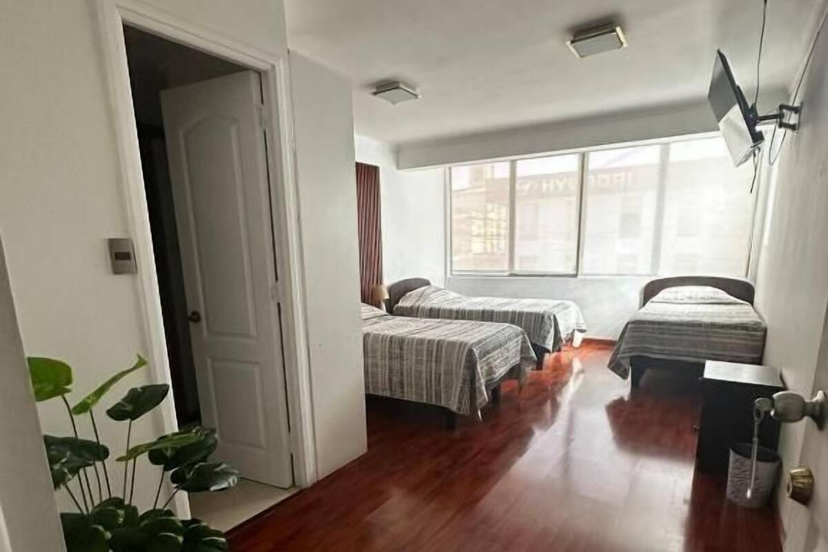 Quarto de hotel com piso de madeira, duas camas, uma janela e uma porta.