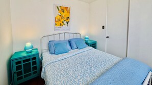Quarto com uma cama, duas mesas de cabeceira, um quadro na parede e uma porta.