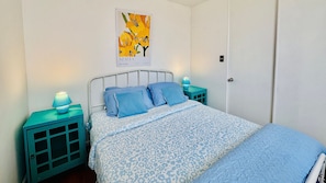 Quarto com uma cama, duas mesas de cabeceira, um quadro na parede e uma porta.