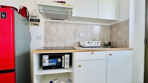 Uma cozinha compacta com micro-ondas, uma pia pequena e uma geladeira vermelha.