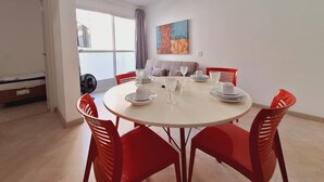 Uma sala de jantar com mesa redonda, cadeiras vermelhas e vista para o exterior através de uma grande janela.