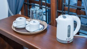 Uma mesa com uma chaleira elétrica Russell Hobbs branca, um prato com duas chávenas brancas e uma colher, e três saleiros e pimenteiros transparentes.