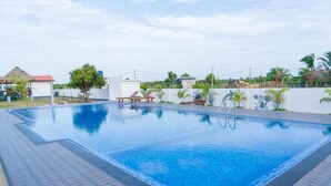 Piscina retangular com borda azulejada, rodeada por um muro de tijolos baixo. Há espreguiçadeiras e uma pequena mesa perto da piscina.