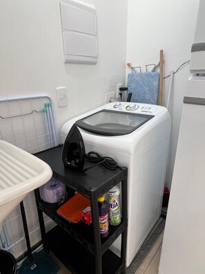 Uma lavanderia compacta com máquina de lavar de carregamento frontal, uma pequena mesa com produtos de limpeza e um radiador.