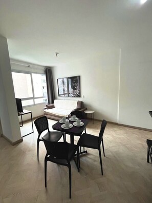 Uma sala de estar moderna com um sofá, uma mesa de jantar com cadeiras, uma mesa redonda pequena e uma janela grande.