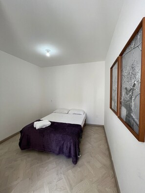 Quarto com cama, colcha roxa e travesseiro branco.