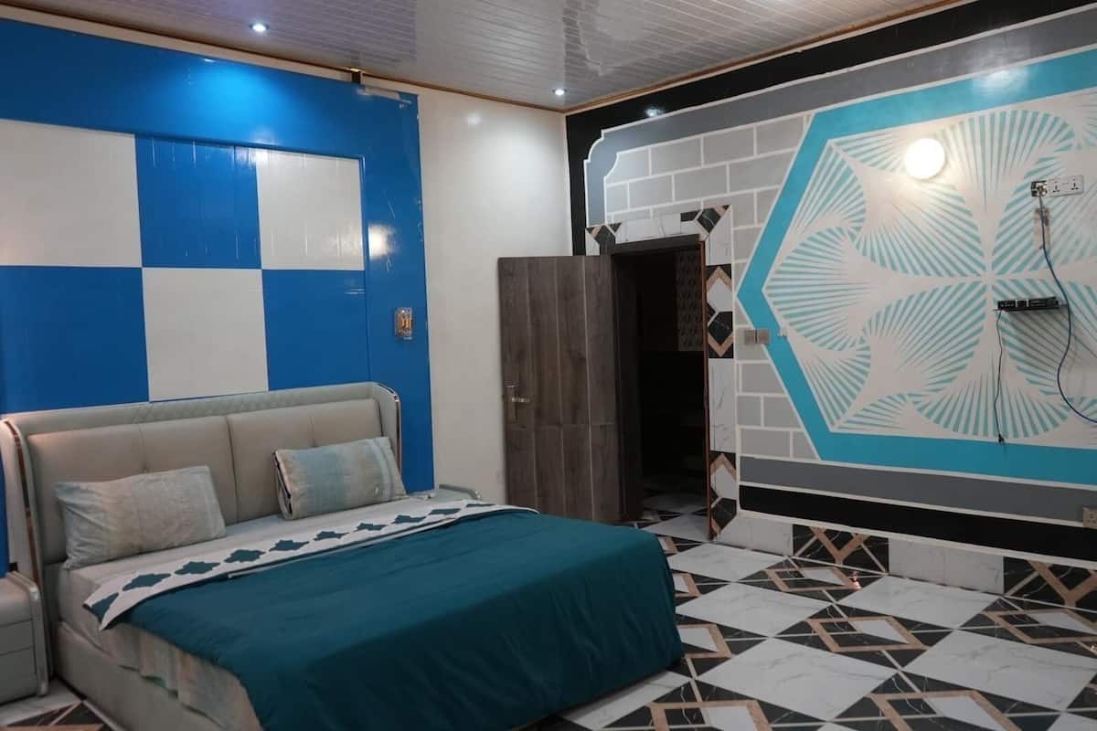 Quarto com cama, guarda-roupa e parede decorativa com padrão geométrico.