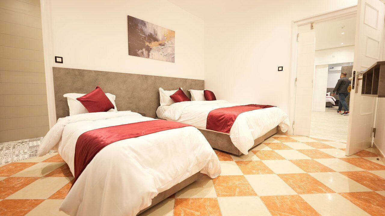 Quarto de hotel com duas camas, um chão quadriculado e um quadro na parede.