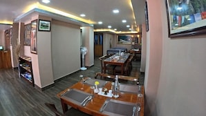 Um saguão de hotel com balcão de recepção, área de refeições com mesas montadas e uma grande moldura na parede.