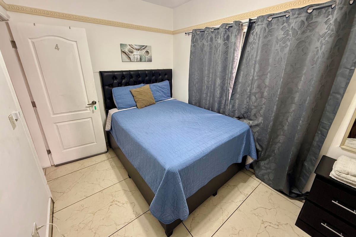 Quarto com cama, porta, obra de arte na parede e cortina.