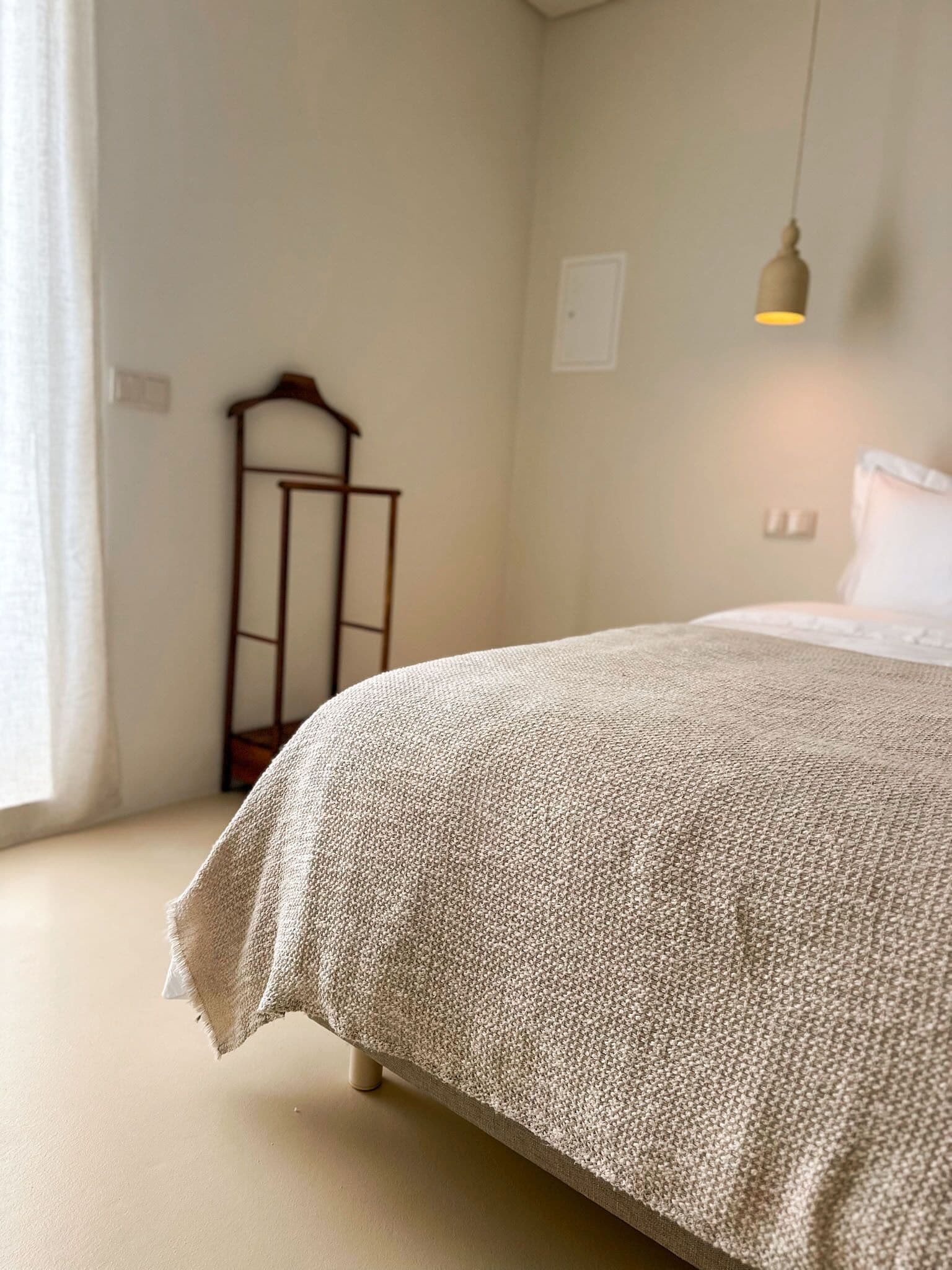 Quarto com cama, luminária pendente e escada de madeira encostada na parede.