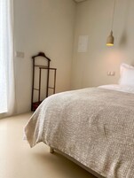Quarto com cama, luminária pendente e escada de madeira encostada na parede.