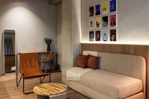 Quarto moderno com sofá, uma cadeira de madeira, uma mesa redonda e uma parede com quadros emoldurados.