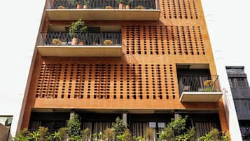 Edifício de vários andares com varandas, plantas em vasos e entrada no nível da rua com assentos.