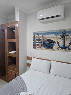 Quarto com cama, guarda-roupa de madeira e pintura com tema praiano na parede.