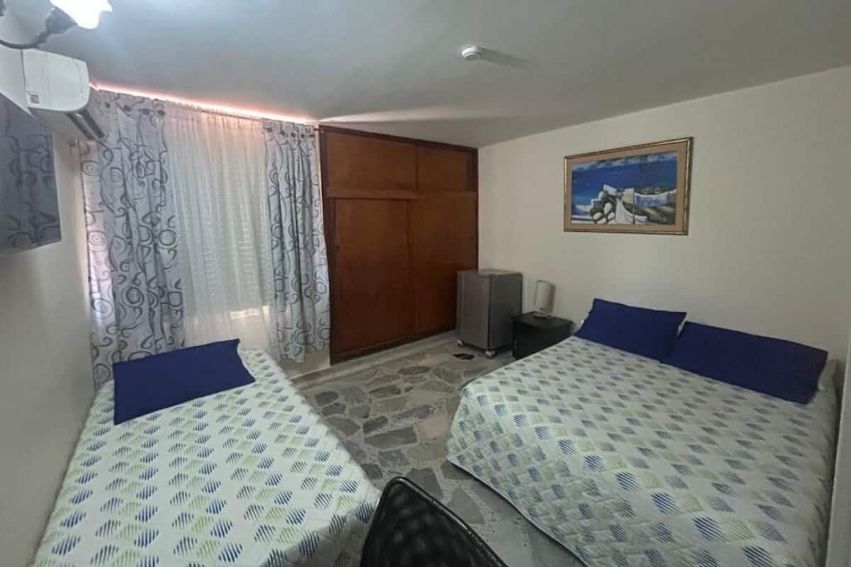 Quarto com duas camas, televisão, quadro e guarda-roupa.