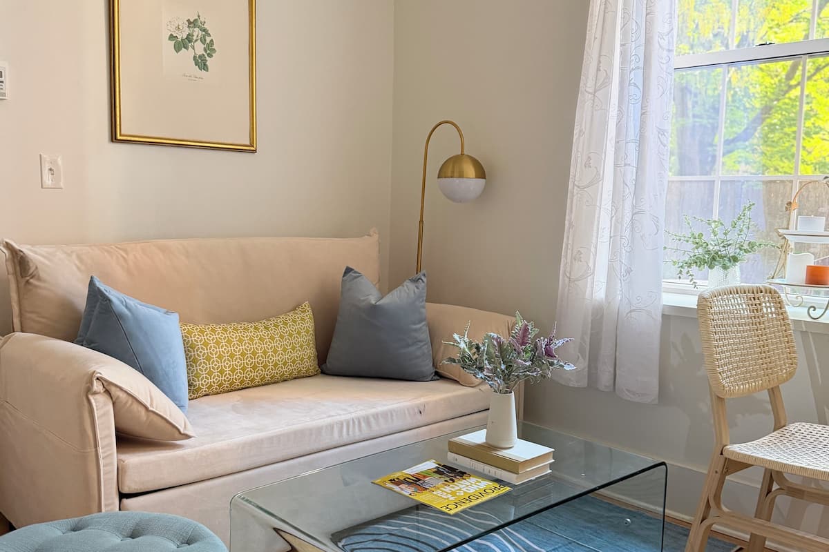 Uma sala de estar moderna com sofá, mesa de centro de vidro, mesa lateral, poltrona e janela com cortinas.