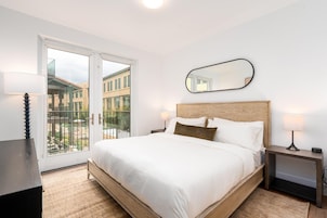 Quarto de hotel com cama, duas mesas de cabeceira com luminárias, um espelho grande e uma porta de vidro deslizante para área externa.