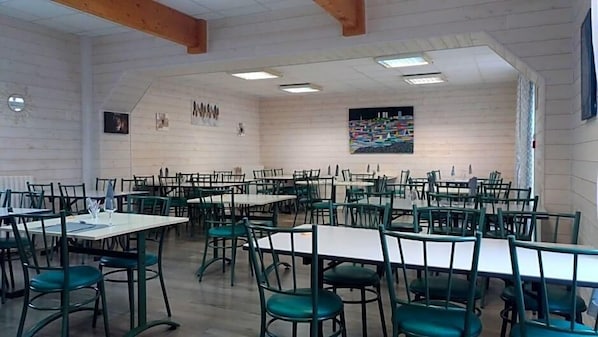 Uma sala de jantar com mesas e cadeiras, um quadro na parede e teto de madeira.