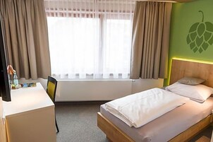 Quarto de hotel com cama, escrivaninha, cadeira, janela com cortinas e parede com o logotipo da Hop.