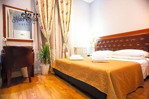 Quarto de hotel com cama, uma cadeira, uma planta em vaso e uma janela com cortinas.