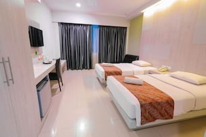 Quarto de hotel com duas camas, uma escrivaninha, uma cadeira e uma televisão.