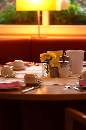 Uma mesa de jantar posta com xícaras de chá, um vaso com flores amarelas e um suporte para cardápio.