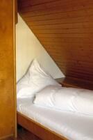 Uma cama de solteiro com roupa de cama branca em um quarto com paredes de madeira e teto inclinado.