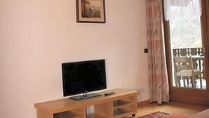 Uma sala de estar com televisão sobre suporte de madeira, tapete estampado, sofá e luminária no teto.