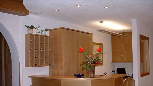 Um balcão de madeira para recepção com um vaso de flores, um espelho e uma prateleira com objetos decorativos.