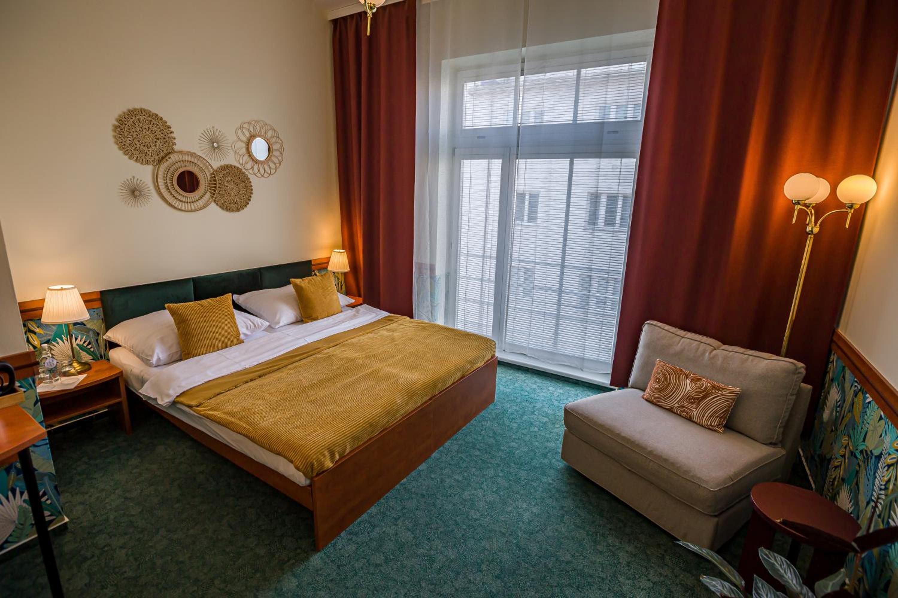 Quarto de hotel com cama, cadeira, mesa de cabeceira, luminária e janela com cortinas.
