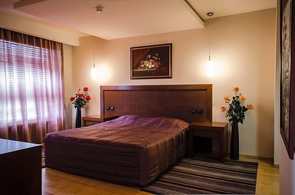 Quarto com uma cama grande, mesas de cabeceira, uma obra de arte emoldurada acima da cama e uma janela com cortinas.
