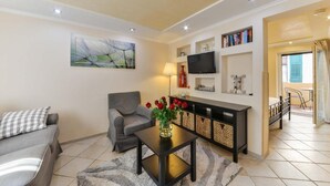 Uma sala de estar com sofá, poltrona, mesa de centro e televisão na parede.