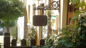 Área externa coberta com grade de metal, uma placa pendurada e plantas em vasos.