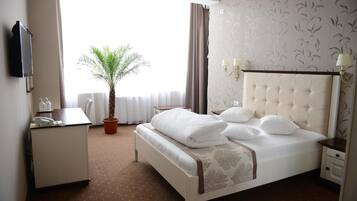 Quarto de hotel com cama, mesa de cabeceira, luminária, planta em vaso e escrivaninha com telefone.