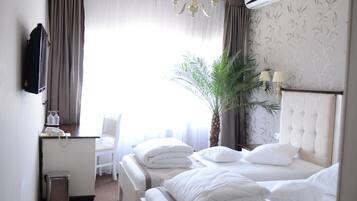 Quarto de hotel com cama, escrivaninha, cadeira, planta e televisão.