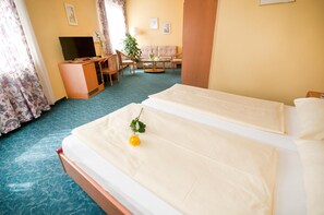 Quarto de hotel com duas camas, uma escrivaninha, uma televisão e um sofá.