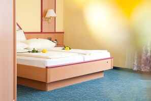 Quarto de hotel com cama, mesa de cabeceira, abajur e janela com cortinas.