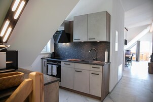 Uma cozinha moderna com forno embutido, pia e fogão. Há uma mesa de jantar de madeira e cadeiras na área de jantar adjacente.
