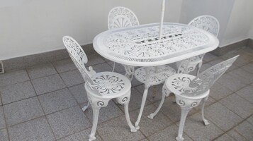 Uma mesa branca para exterior e quatro cadeiras a combinar, com desenhos detalhados, apoiadas em um chão de azulejos.