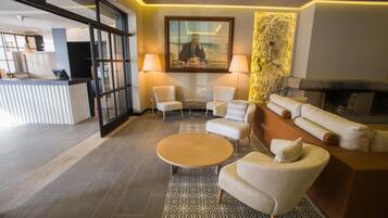 Um lobby de hotel moderno com balcão de recepção, área de estar com sofás e poltronas, um tapete estampado e uma lareira.