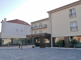 Um hotel com fachada moderna, entrada coberta e um pátio de paralelepípedos.