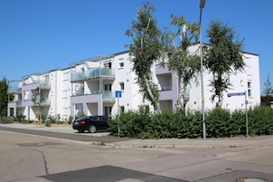 Um prédio de apartamentos moderno com varandas, uma rua na frente e um carro estacionado no lado.