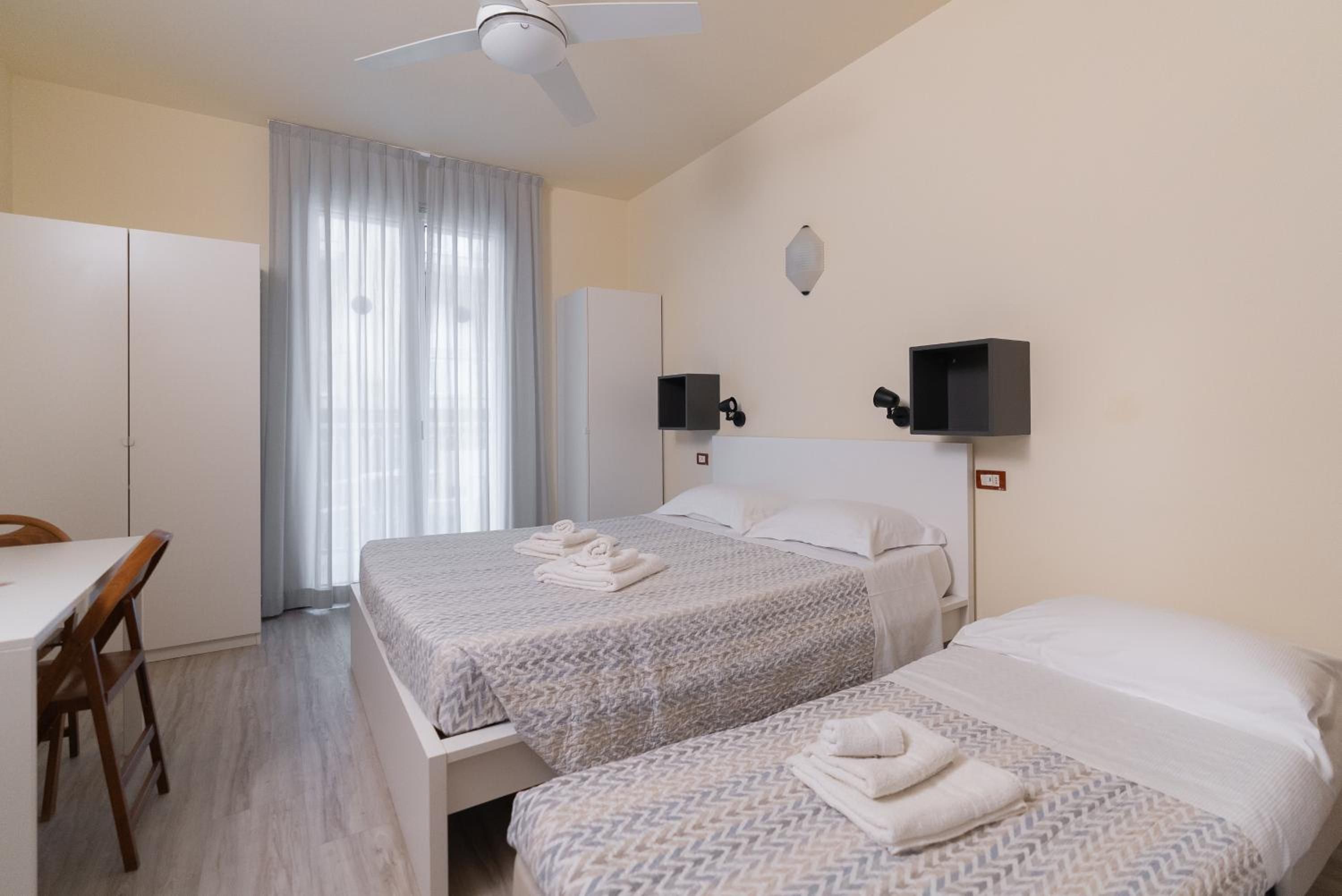 Quarto de hotel com duas camas, uma escrivaninha e uma cadeira.
