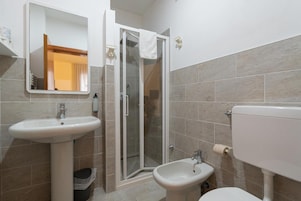 Casa de banho com lavatório, bidé, sanita e cabine de duche com portas de vidro.
