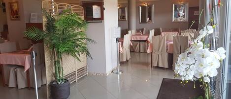 Um saguão de hotel com balcão de recepção, área de estar e uma grande planta em vaso.
