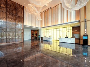 Um hall amplo com piso de mármore refletivo, um balcão de recepção e uma parede decorativa com padrões elaborados.