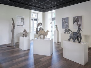 Uma galeria de arte com esculturas expostas, pedestais brancos e cartazes informativos.