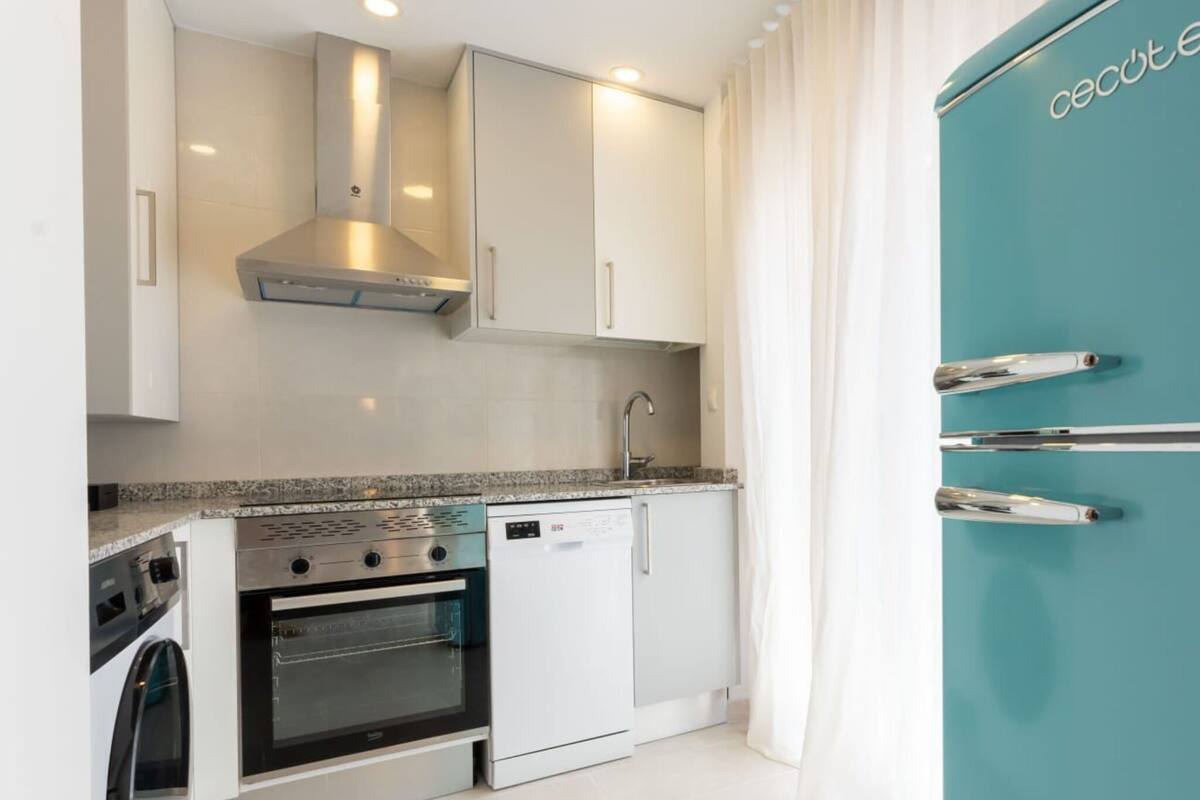Uma cozinha moderna com forno embutido, máquina de lavar e uma geladeira azul-turquesa.