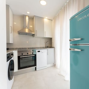 Uma cozinha moderna com forno embutido, máquina de lavar e uma geladeira azul-turquesa.